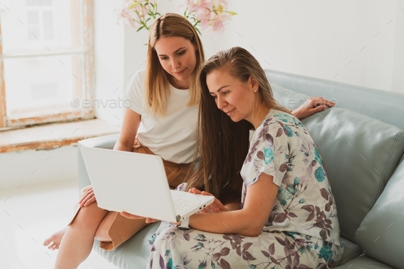 two adorable young women chatting at home on the couch, drinking coffee ...