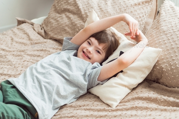 Dpwn syndrome boy raising hands up laying on bed Stock Photo by shapoval08