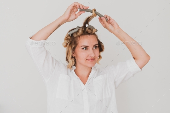 Charming young woman caring for her hair by winding curlers. Stock ...