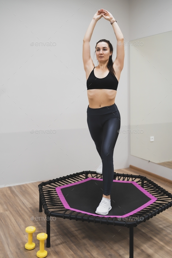 Flexible athletic woman on sports trampoline doing stretching exercises ...