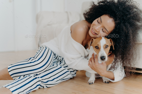 Affectionate young woman hugs dog with love and care, keeps eyes closed ...