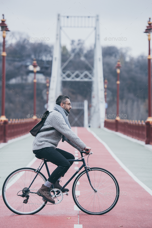 handsome adult man riding bicycle on pedestrian bridge on cloudy day ...