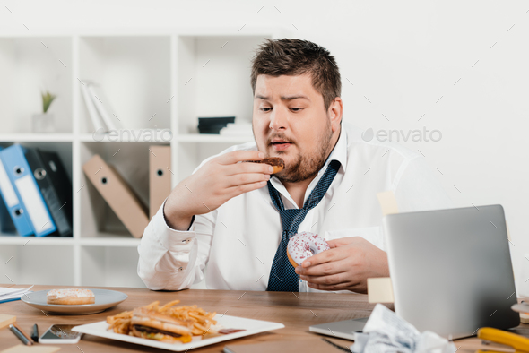 overweight businessman eating donuts, hamburger and french fries at ...