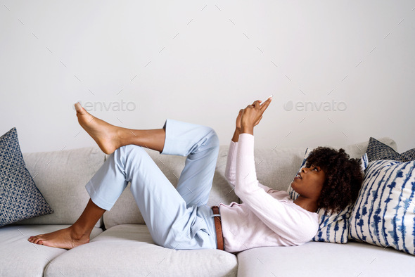 Beautiful black woman with the Afro hair laying down on the couch using ...