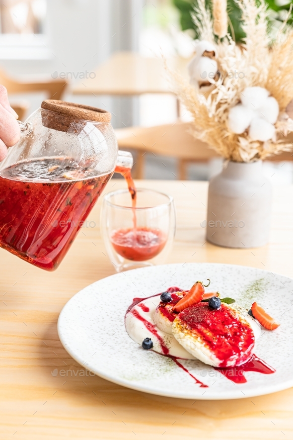 Process of pouring hot red tea into cup from a transparent teapot. Cafe ...