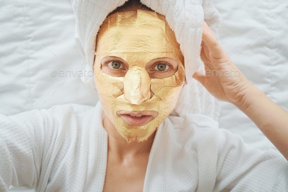 Selfie of the woman wearing a golden facemask wearing Bath robe and a ...