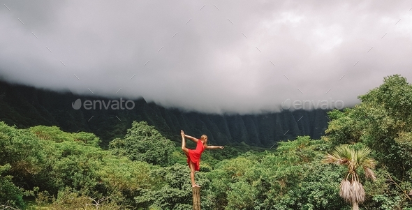 Woman on a red dress doing yoga pose balancing against dramatic ...