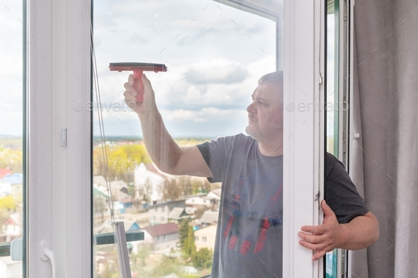Caucasian elderly man washing a window with a brush and detergent in ...