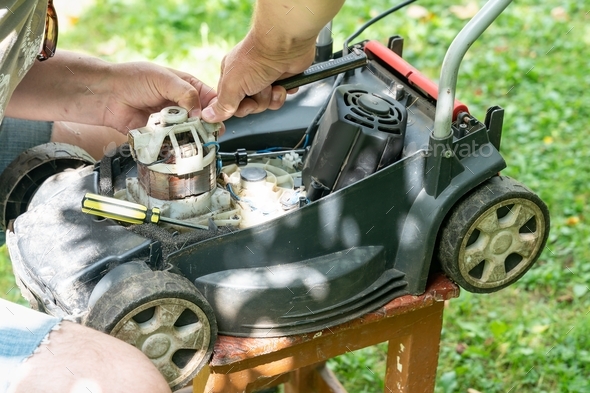 Repairman fixes the lawn mower engine with tools at the workshop ...
