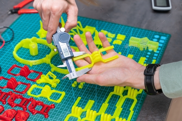 A man measures the dimensions of a 3D printed part with a caliper ...