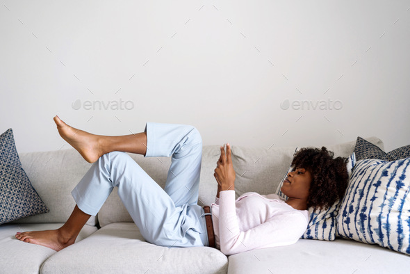 Beautiful black woman with the Afro hair laying down on the couch using ...