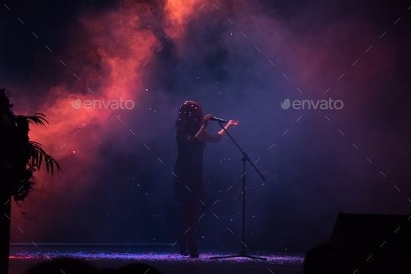 Singer on stage in dark blue and purple spotlights singing in front of ...