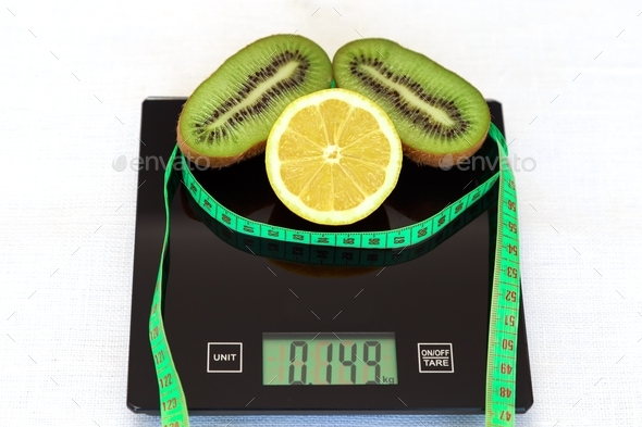 half-cut kiwi and lemon lying on black kitchen scales on white ...