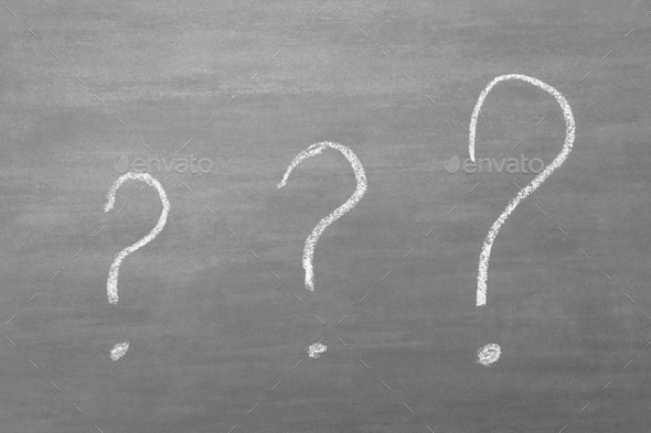 Question marks of different sizes are drawn with chalk on a gray board ...