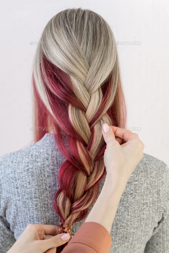 The hairdresser makes the girl's hair - braids a multi-colored braid ...