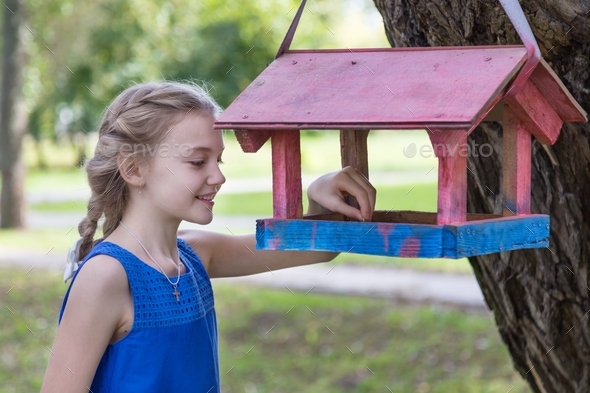 Caucasian girl pouring food into wooden bird feeder in public park ...