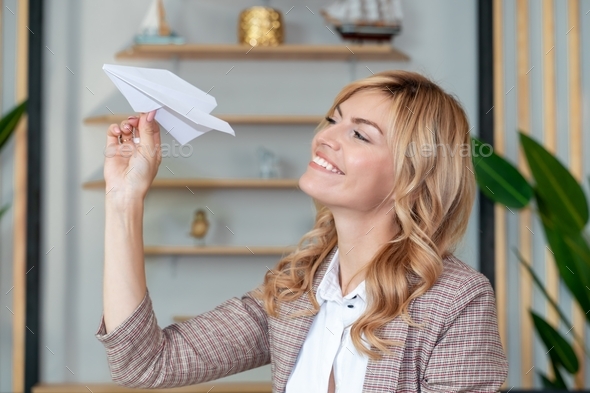 Caucasian young woman throwing paper plane into the air indoor closeup ...