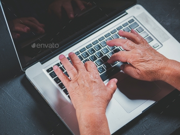 Grandmother works behind laptop, typing on keyboard with her old hands ...