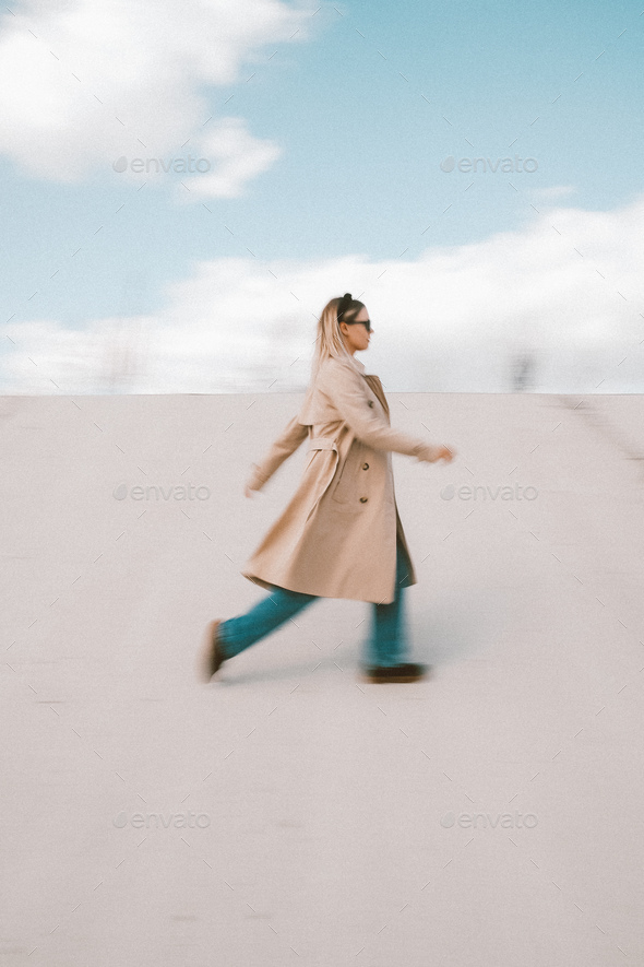 Pretty woman in trench coat on sky background. She walking fast ...