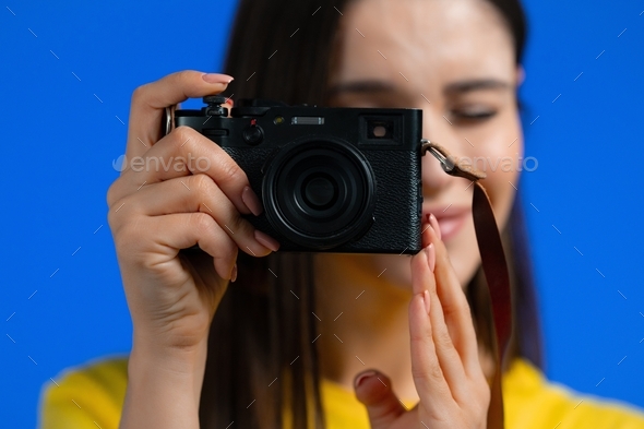 Young pretty woman takes pictures with DSLR camera over blue background ...