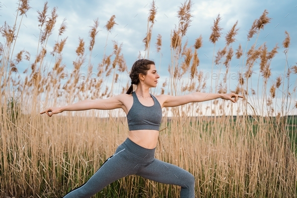 European woman doing yoga exercise on reed natural background ...