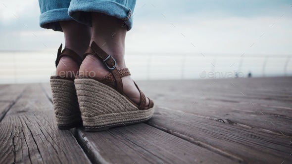 Female feet in beautiful style boho wedge shoe standing on wooden beach ...