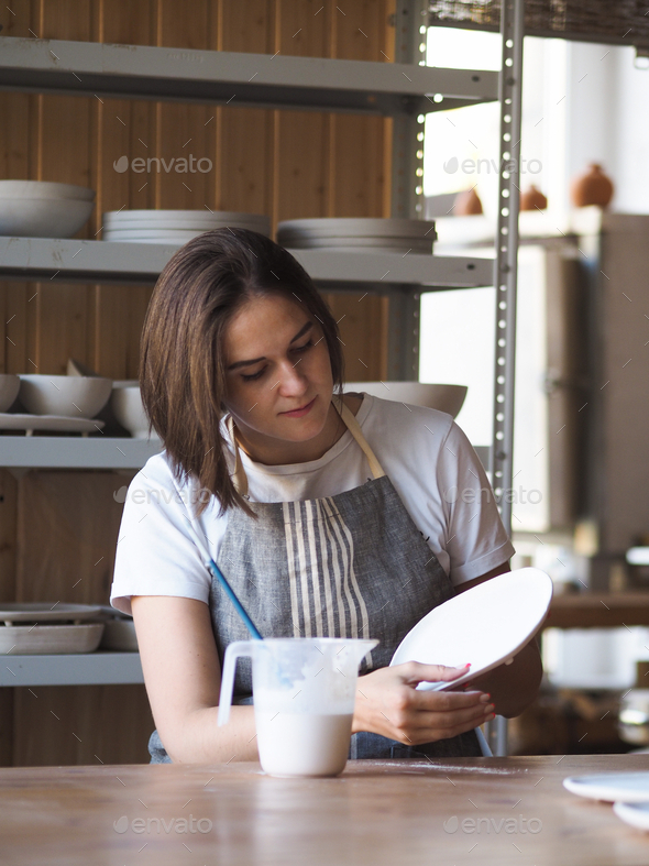 Young woman ceramicist with short hair making clay plate in her ...
