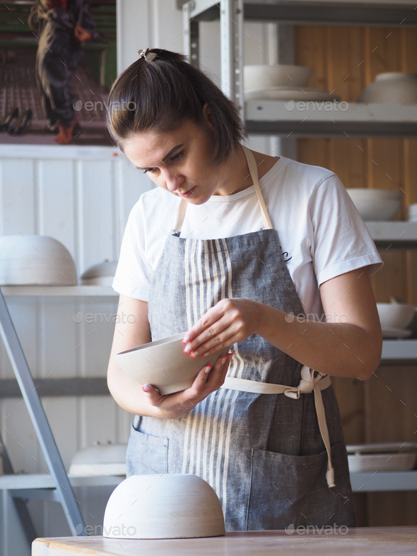 Young woman ceramicist with short hair making clay plate in her ...