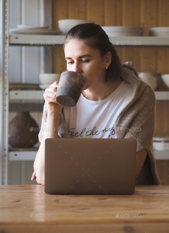 Portrait of beautiful serious woman working on laptop and drinking ...