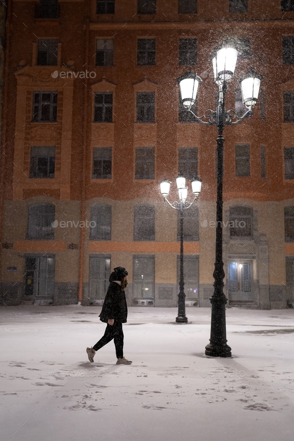 Man walking along snowy empty night city street after heavy snowstorm ...
