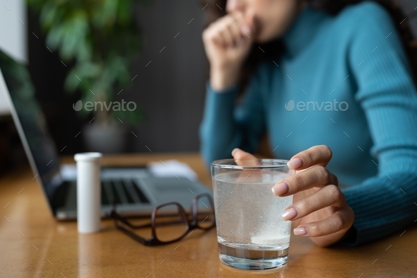 Closeup of painkiller dissolving in glass of water. Sick business woman ...