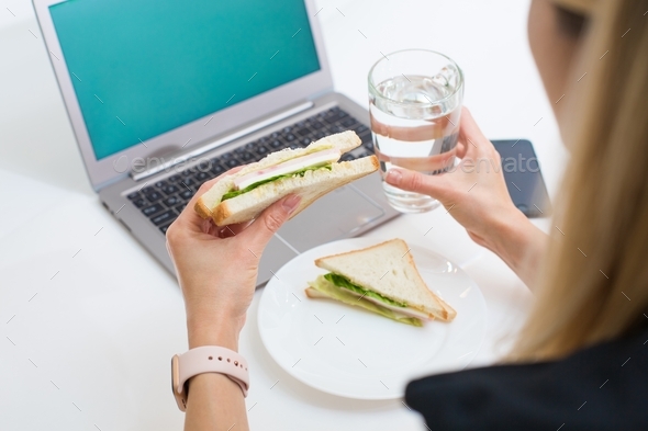 Woman eating a breakfast sandwich while working with a laptop ...