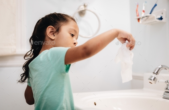 Diverse pre school girl at home practicing good hygiene, washing hands ...