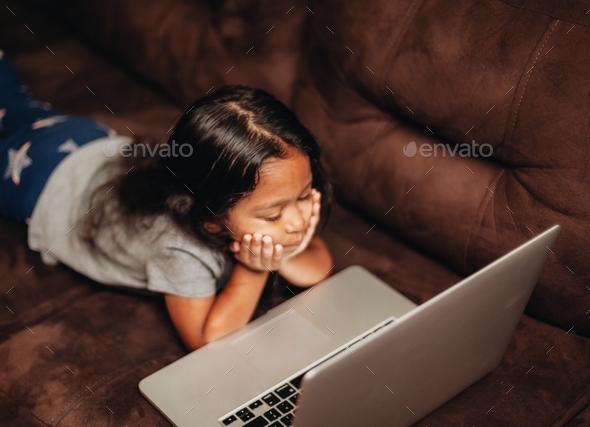 Diverse pre school girl at home on the couch using a laptop computer ...
