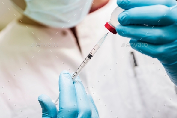African American doctor drawing up solution from vial into syringe ...
