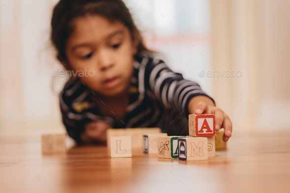 Diverse pre-k girl at home on hardwood floor playing with wooden letter ...