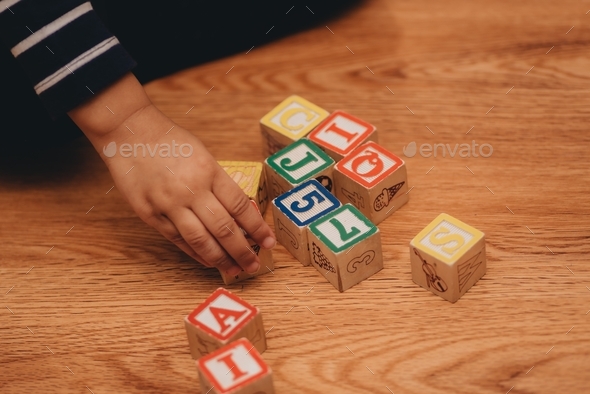 Diverse pre-k girl at home on hardwood floor playing with wooden letter ...