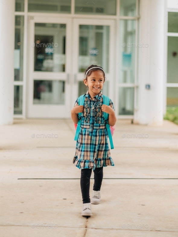 happy diverse pre school girl walking out of school building with bag ...
