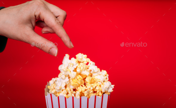 woman taking popcorn from bucket against red background Stock Photo by ...