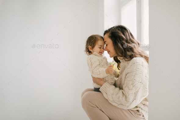 Young mother and her little baby snuggling and having fun sitting near ...