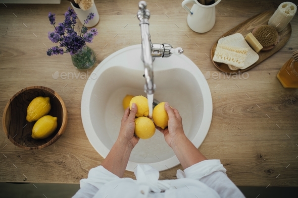 Young woman washing lemons in a sink to make fresh lemonade. Zero waste ...