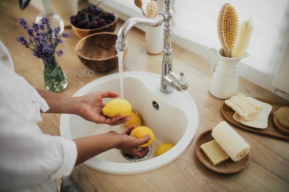 Young woman washing lemons in a sink to make fresh lemonade. Zero waste ...