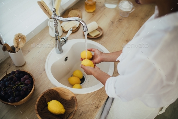 Young woman washing lemons in a sink to make fresh lemonade. Zero waste ...