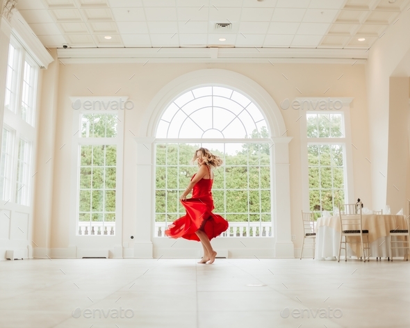 Young millennial woman in a red dress happily dancing in a large open ...
