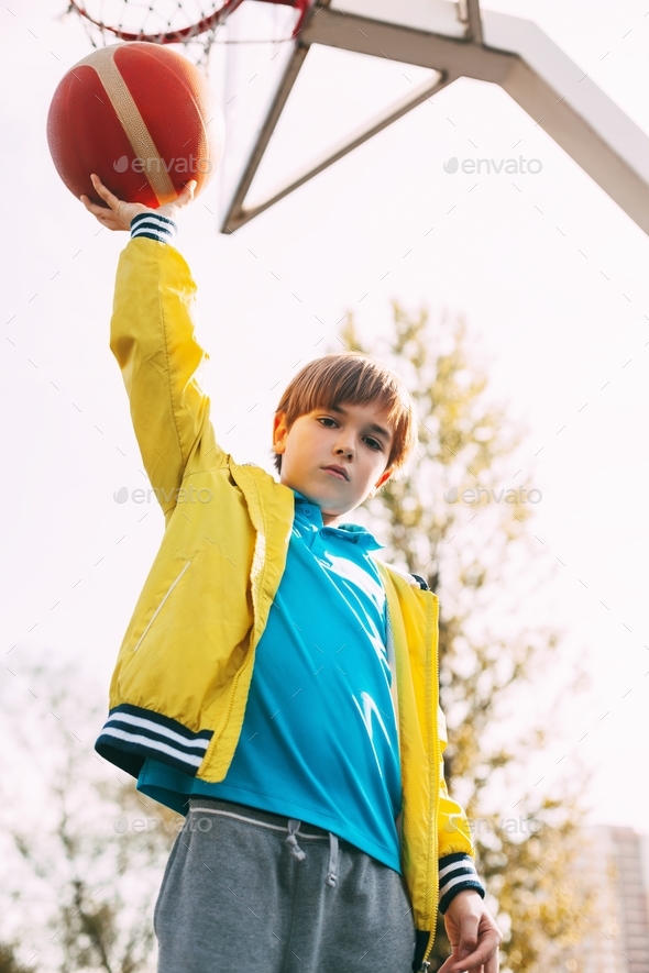 Portrait of a cute boy basketball player standing with a ball in his ...