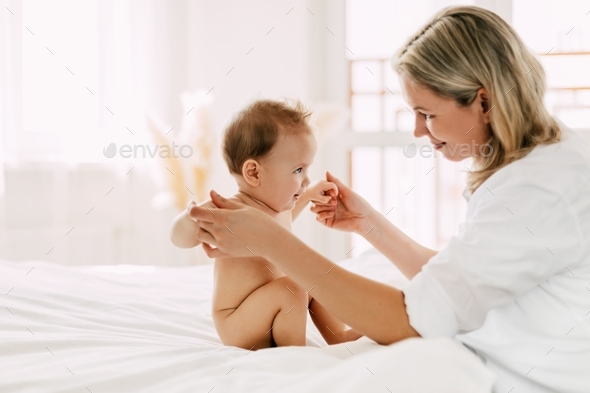 A cute baby is sitting on the bed with her arms outstretched and ...