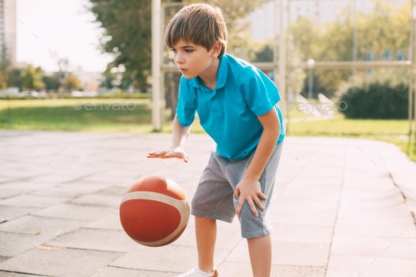 Focused cute boy athlete leads the ball in a game of basketball. A boy ...