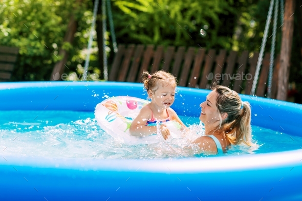 Cheerful healthy mother and daughter play in swimsuits in the pool ...