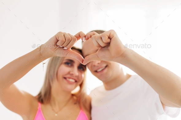 A couple stands close, hugging, making a heart shape with their hands ...