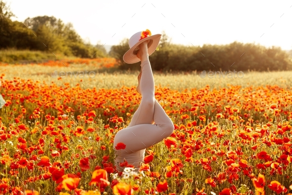 Close up of the legs of a girl doing yoga with a hat on a poppy field ...